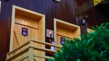 Um edifício de madeira com duas portas numeradas 09 e 10, uma pequena varanda e um arbusto verde em primeiro plano.
