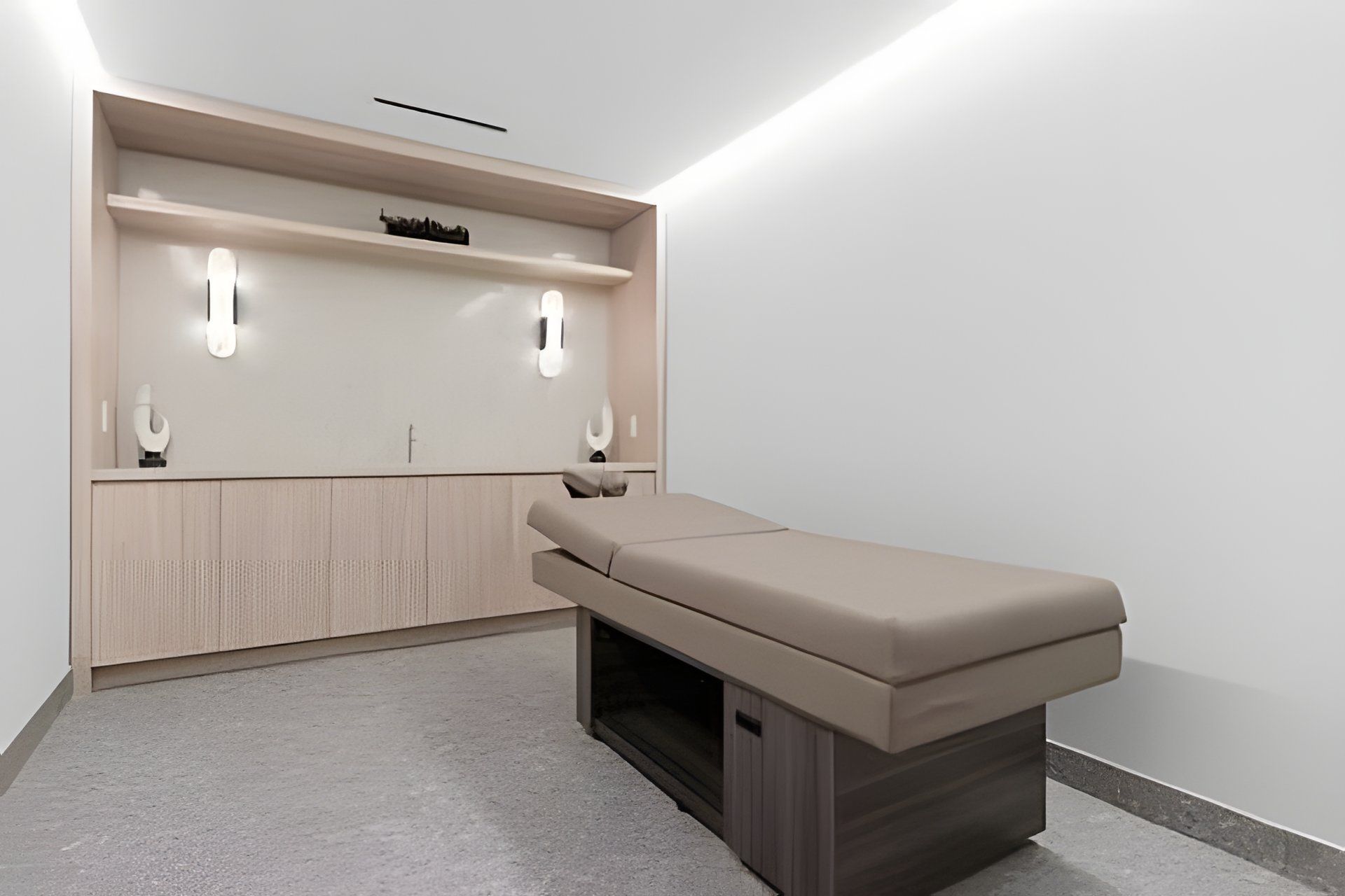 Sala de exames médicos com uma mesa de exame individual, armários de madeira e dois armários fixos na parede com painéis iluminados.