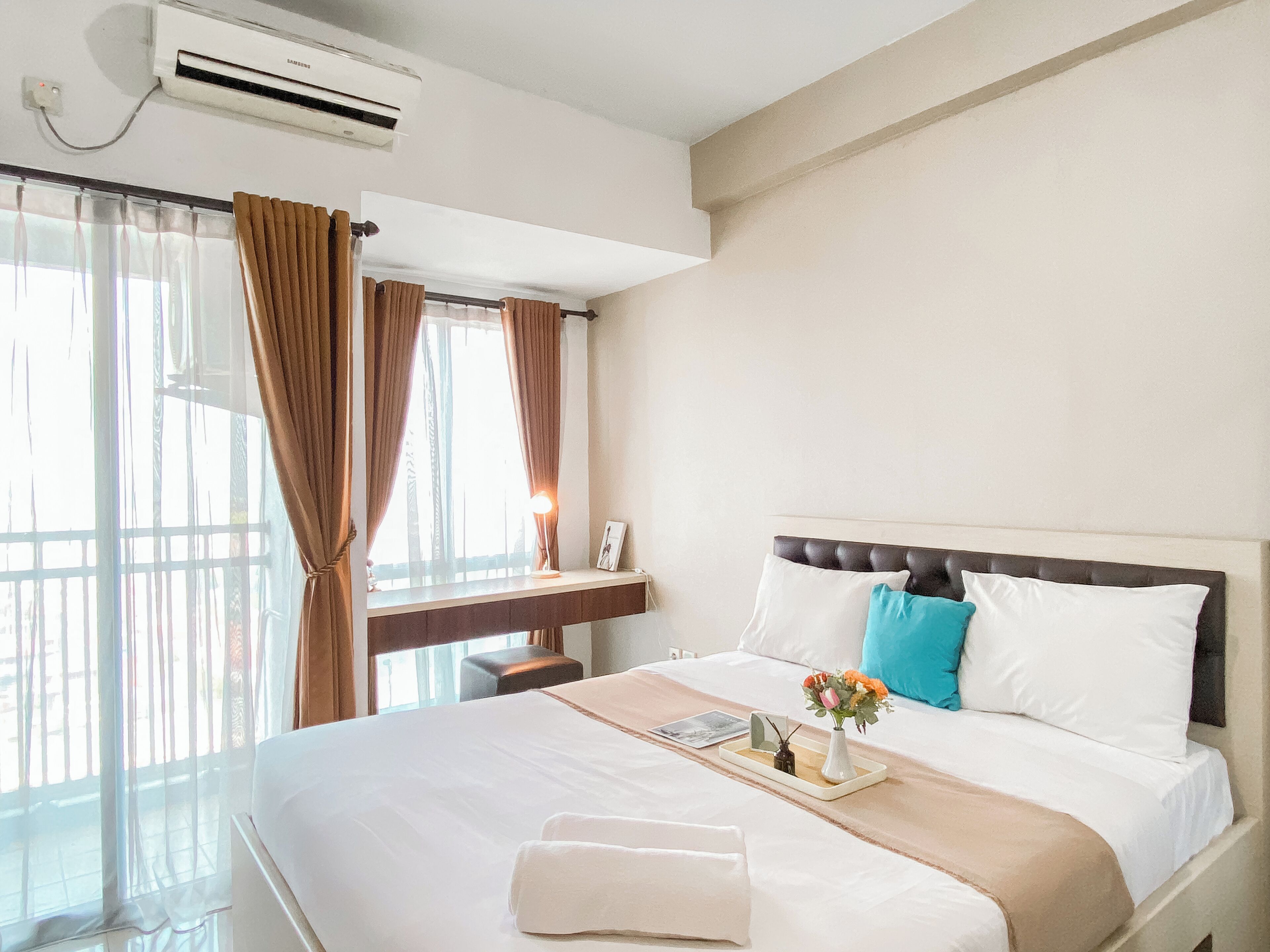 Quarto de hotel com cama, mesa de cabeceira, escrivaninha e janela com cortinas.