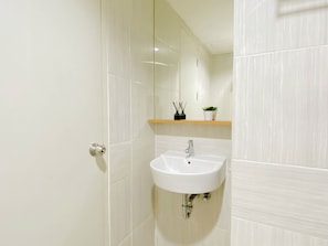 Casa de banho com lavatório branco, espelho e prateleira com planta e recipiente.