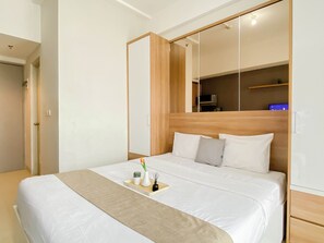 Cama bem arrumada com cabeceira de madeira e mesa de cabeceira com um suporte contendo um vaso e um livro.
