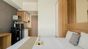 Quarto de hotel com cama, mesa de cabeceira e cozinha compacta equipada com micro-ondas, geladeira e forno.
