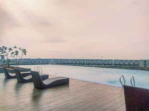 Área na piscina com espreguiçadeiras e vista para um edifício moderno do outro lado da água.