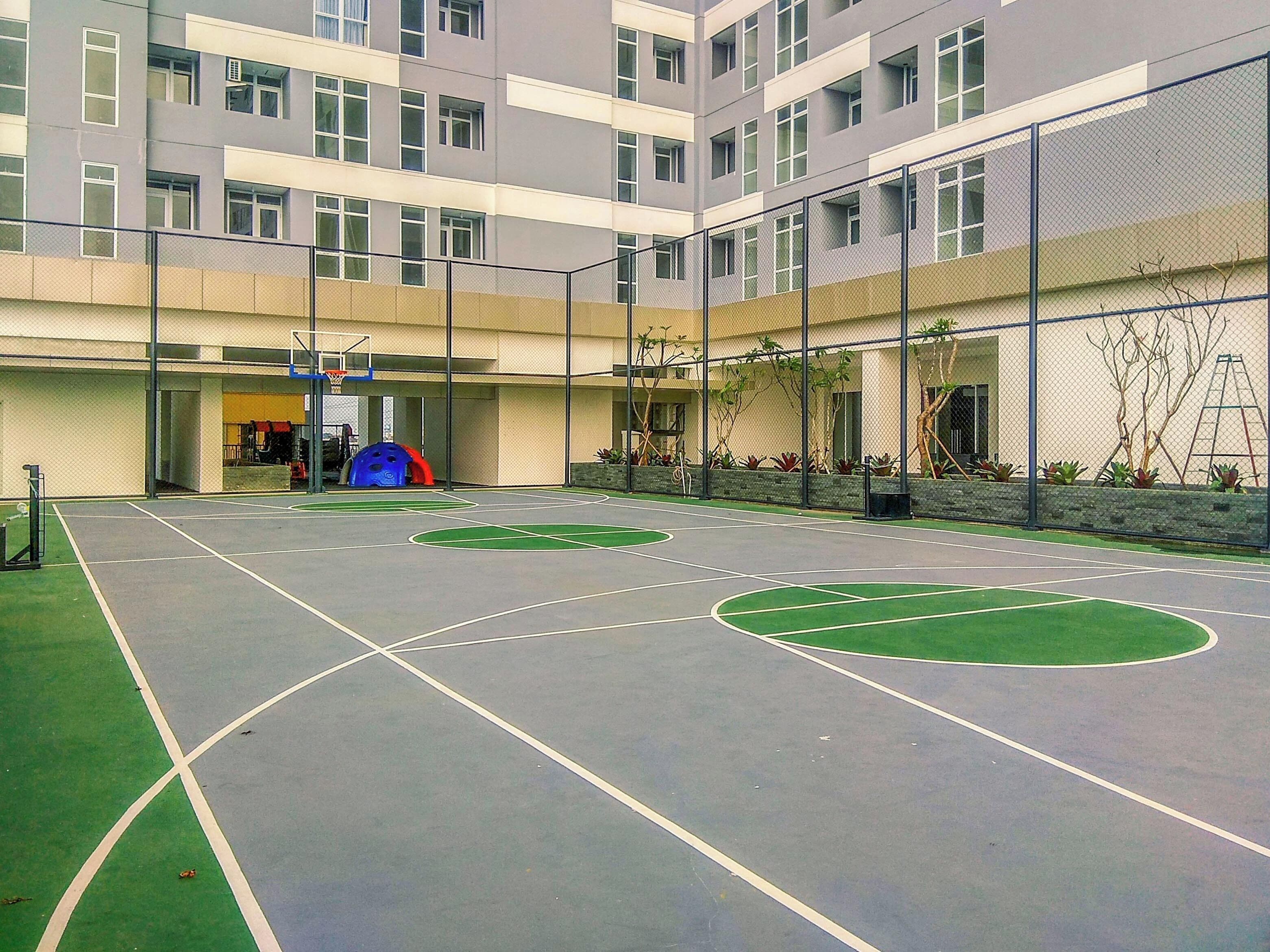 Uma quadra de basquete interna com uma estrutura de recreação azul e vermelha, cercada por um edifício com várias janelas e uma área cercada.