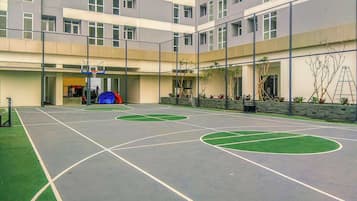 Uma quadra de basquete interna com uma estrutura de recreação azul e vermelha, cercada por um edifício com várias janelas e uma área cercada.