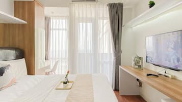 Quarto de hotel com cama, escrivaninha, televisão de tela plana, ar condicionado e janela com cortinas.