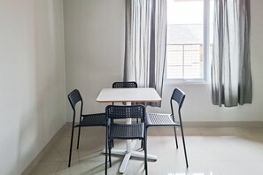 Uma área de refeições com mesa e quatro cadeiras, janela com cortinas e piso ladrilhado.