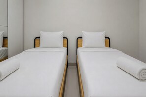 Duas camas de solteiro com estrutura de madeira e roupa de cama branca, num quarto com paredes simples e um espelho.