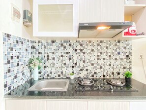Uma cozinha com revestimento de azulejos, pia de aço inoxidável e fogão a gás.