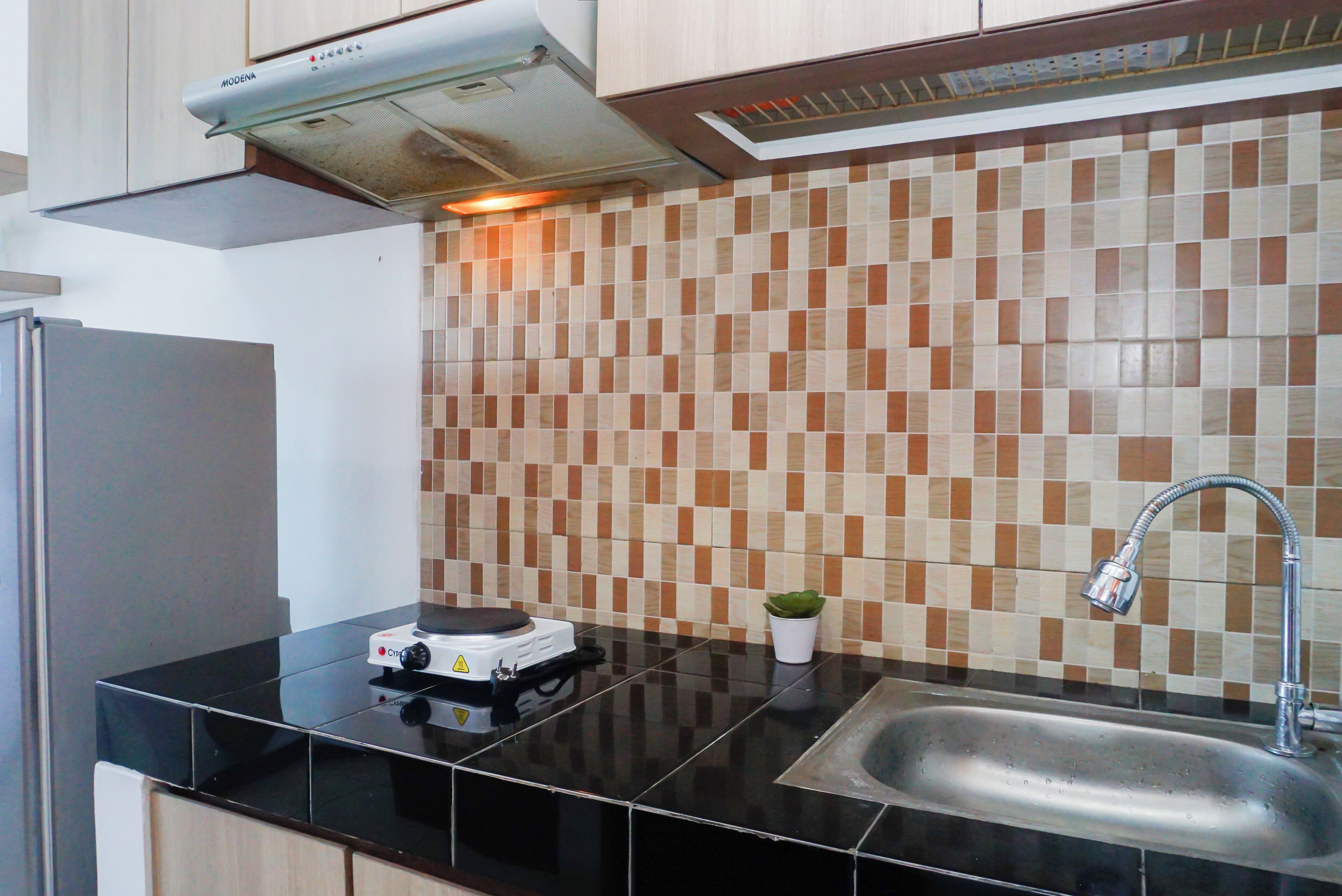 Cozinha com bancada preta, pia, fogão e painel de azulejos.