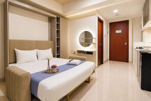 Quarto de hotel com cama, mesa de cabeceira, espelho, guarda-roupa e uma pequena cozinha.