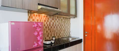Uma cozinha com geladeira rosa, painel de azulejos e armário de madeira sobre o fogão.