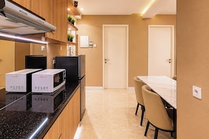 Cozinha compacta com eletrodomésticos embutidos, área de jantar com mesa e cadeiras, e uma porta que dá acesso a outro cômodo.