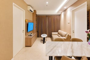 Quarto de hotel moderno com televisão de tela plana, sofá, mesa redonda pequena e mesa de jantar com tampo de mármore.