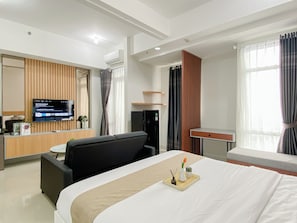 Quarto de hotel com uma cama, escrivaninha com computador, televisão na parede e janela com cortinas.