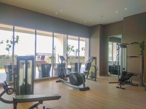 Uma academia moderna com diversos equipamentos de exercício, amplas janelas e vista para plantas ao ar livre.