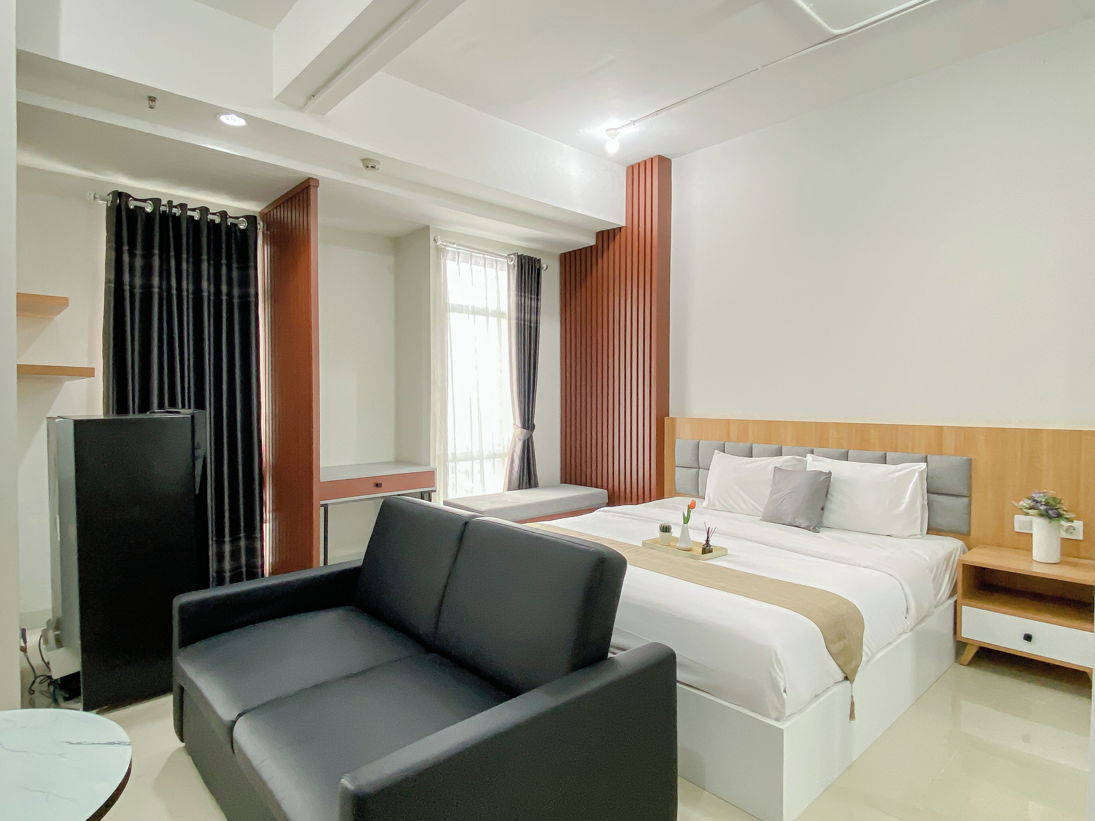 Quarto de hotel moderno com cama, sofá, TV e mesa de cabeceira.