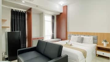 Quarto de hotel moderno com cama, sofá, TV e mesa de cabeceira.