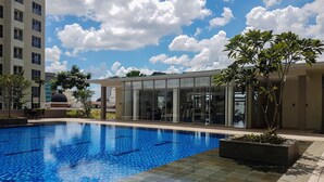 Uma piscina com superfície de água azul cristalina, rodeada por um deck ladrilhado.