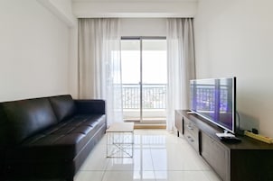 Uma sala de estar moderna com um sofá de couro preto, uma TV de tela plana em um armário de madeira e uma porta de vidro deslizante que dá para uma varanda.