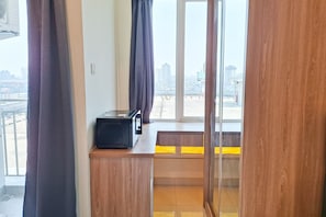 Quarto com vista para a paisagem urbana através de grandes janelas, um banco de madeira e uma pequena mesa com um objeto preto.