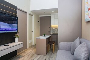 Espaço compacto com televisão na parede, cozinha pequena e área de estar com sofá.