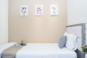 Quarto com cama, almofadas, mesa de cabeceira com uma revista e três obras de arte penduradas na parede.
