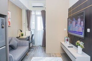 Uma sala de estar moderna com um sofá cinza, uma mesinha com abajur, uma TV fixada na parede e um vaso de planta em uma mesinha lateral.