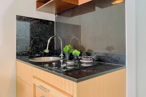 Cozinha com bancada de mármore preto, pia de aço inoxidável, fogão a gás e uma pequena planta em vaso.