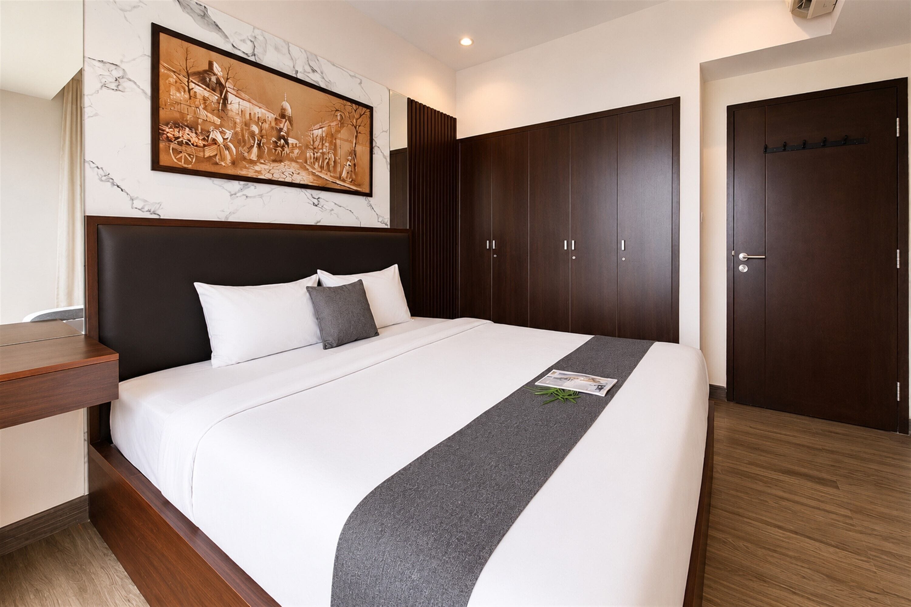 Quarto de hotel com uma cama grande, guarda-roupa de madeira escura e parede de mármore com um quadro emoldurado.