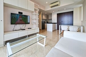 Uma sala de estar moderna com televisão de tela plana, uma mesa de centro de vidro e um sofá.