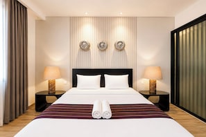 Quarto de hotel com uma cama grande, duas mesas de cabeceira, um encosto de cama e três luminárias fixadas na parede.
