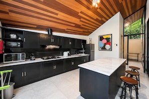 Cozinha moderna com ilha central, armários pretos e teto de madeira.