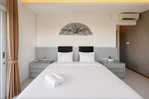 Quarto de hotel com uma cama grande, duas mesas de cabeceira, ar condicionado fixado na parede e uma cortina à esquerda.