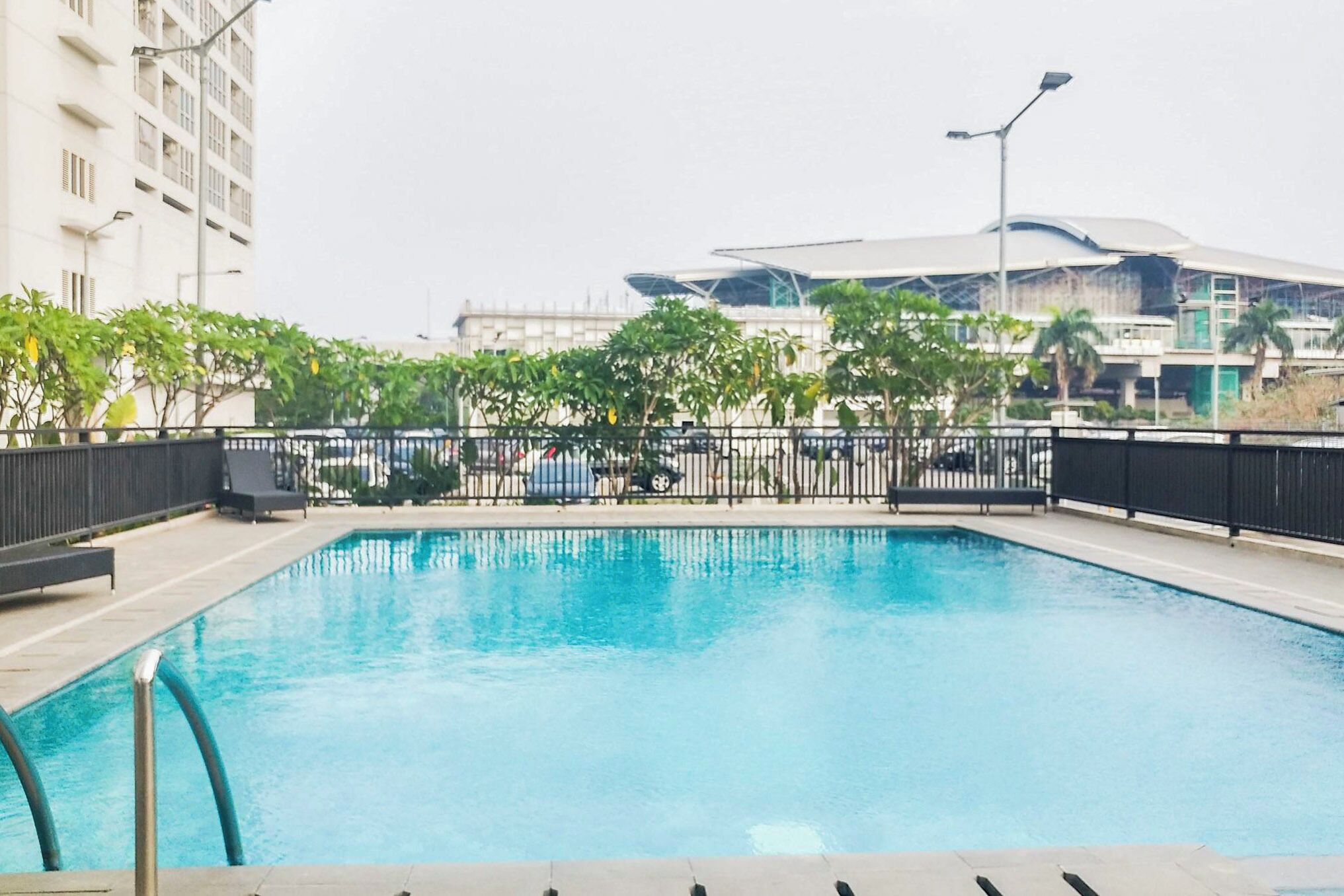Piscina ao ar livre com grade de metal, cercada por árvores e um muro.