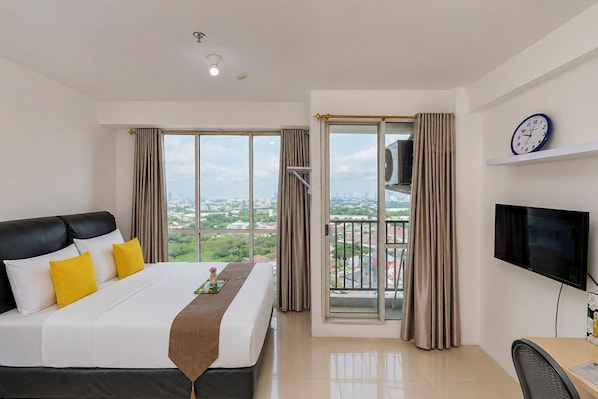 Quarto de hotel com cama, televisão, escrivaninha e varanda com vista para a cidade.