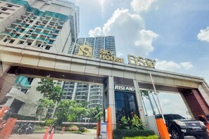 Entrada de hotel com uma placa grande, uma entrada com portão e um edifício moderno ao fundo.