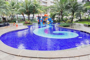 Uma piscina com design em espiral, rodeada por palmeiras e uma área de recreação infantil.