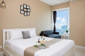 Quarto de hotel com cama, uma cadeira, janela com vista para edifícios e parede com quadros emoldurados.