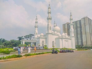 Uma mesquita com vários minaretes e cúpulas, cercada por vegetação e uma área de estacionamento com motocicletas.
