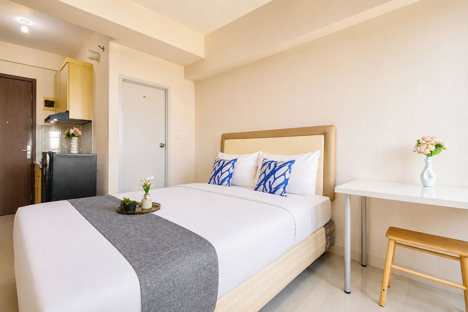 Quarto de hotel com uma cama, uma pequena mesa, uma cadeira, um frigorífico e uma porta.