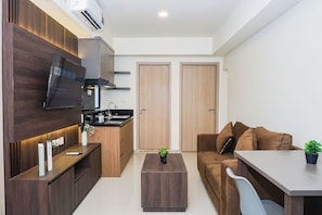 Um espaço compacto com cozinha compacta, um sofá, uma mesa de centro e uma TV fixada na parede.