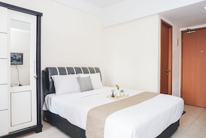 Quarto de hotel com cama, guarda-roupa, porta e uma pequena mesa com um vaso e uma planta.