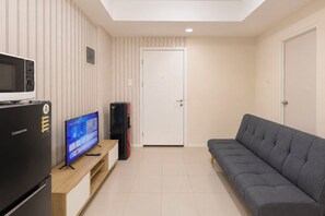 Uma sala de estar moderna com televisão de tela plana, geladeira, computador e sofá cinza.
