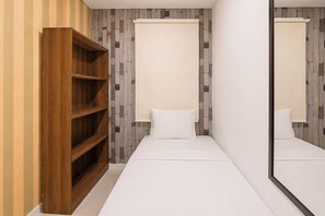 Quarto pequeno com um guarda-roupa de madeira, uma cama com roupa de cama branca e um espelho refletindo o quarto.