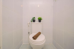 Casa de banho com sanita branca, uma toalha no assento e duas plantas em vasos sobre o tanque.