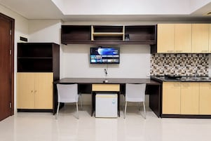 Cozinha compacta com TV integrada, duas cadeiras brancas e um frigorífico pequeno.