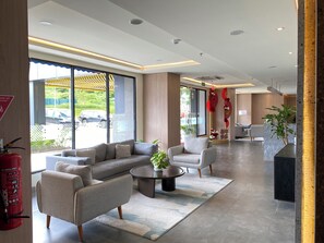 Um saguão de hotel moderno com um sofá, cadeiras, uma mesa de centro e um balcão de recepção.