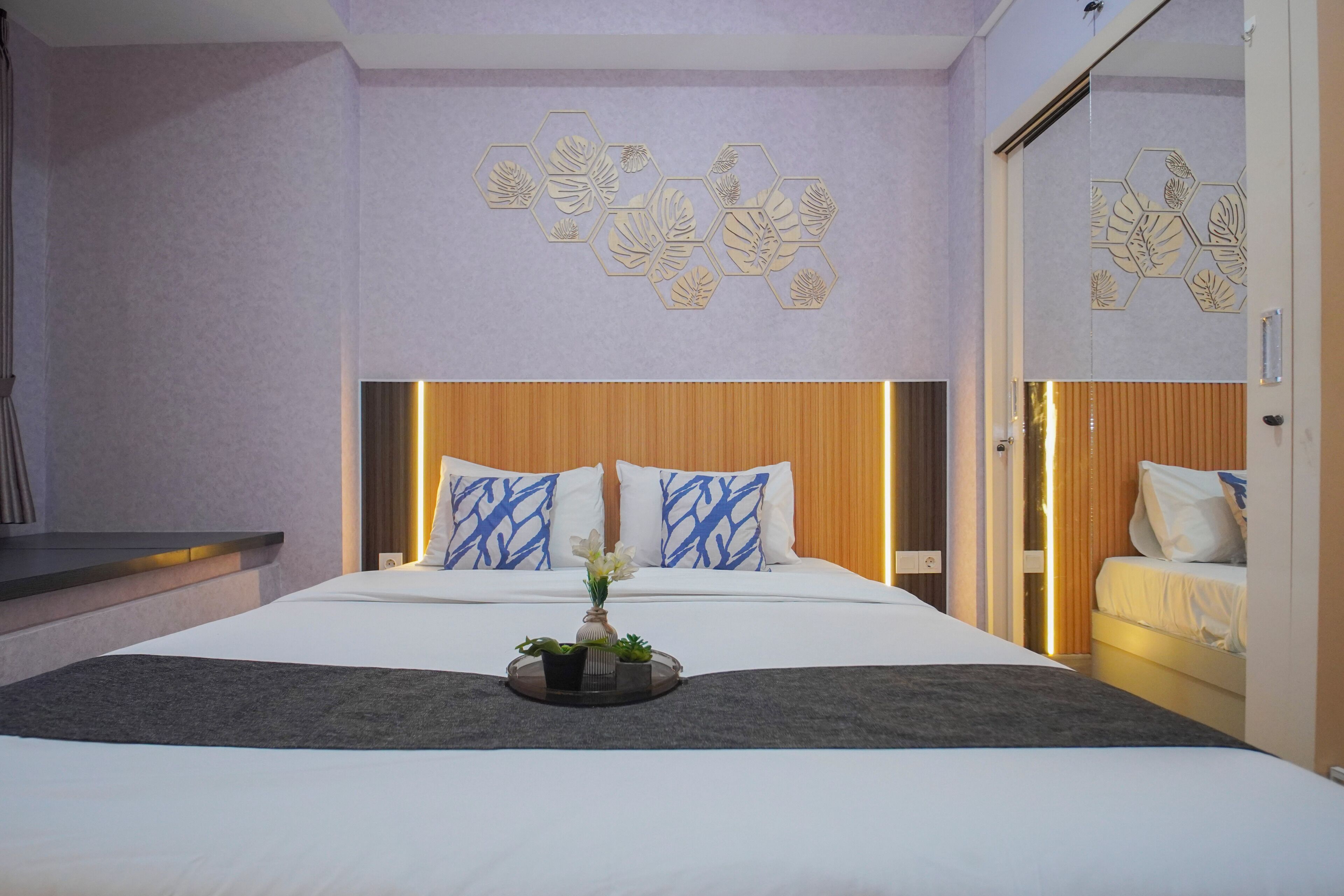 Quarto de hotel com uma cama grande, cabeceira de madeira e painel decorativo na parede.