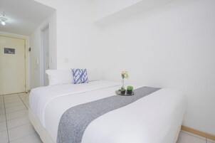 Quarto de hotel com cama, mesa de cabeceira com um vaso de flores e porta com uma placa.